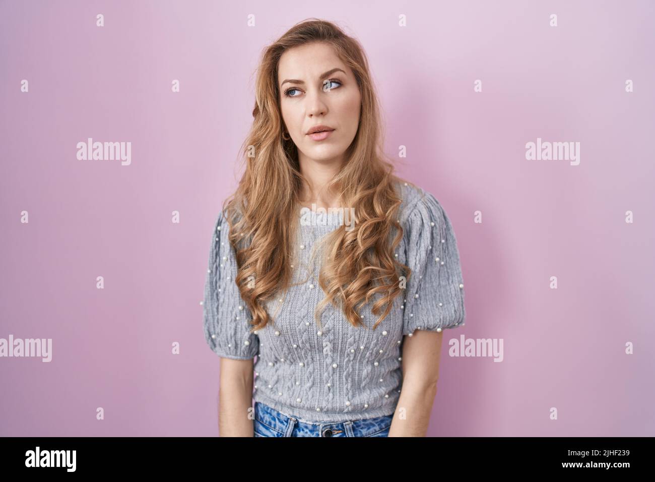 Beautiful blonde woman standing over pink background looking sleepy and ...