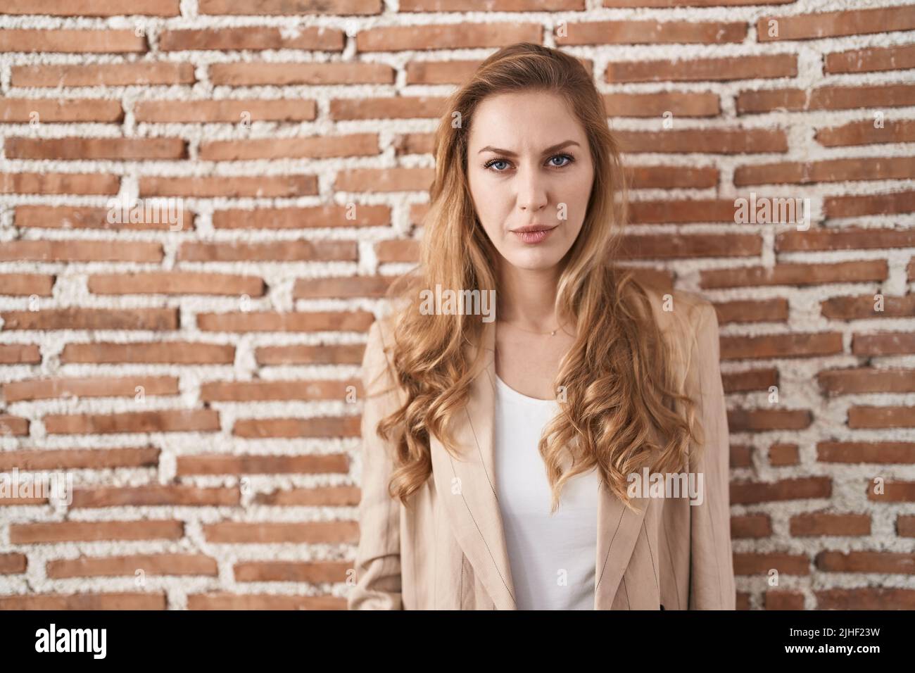 Beautiful blonde woman standing over bricks wall depressed and worry for distress, crying angry ...