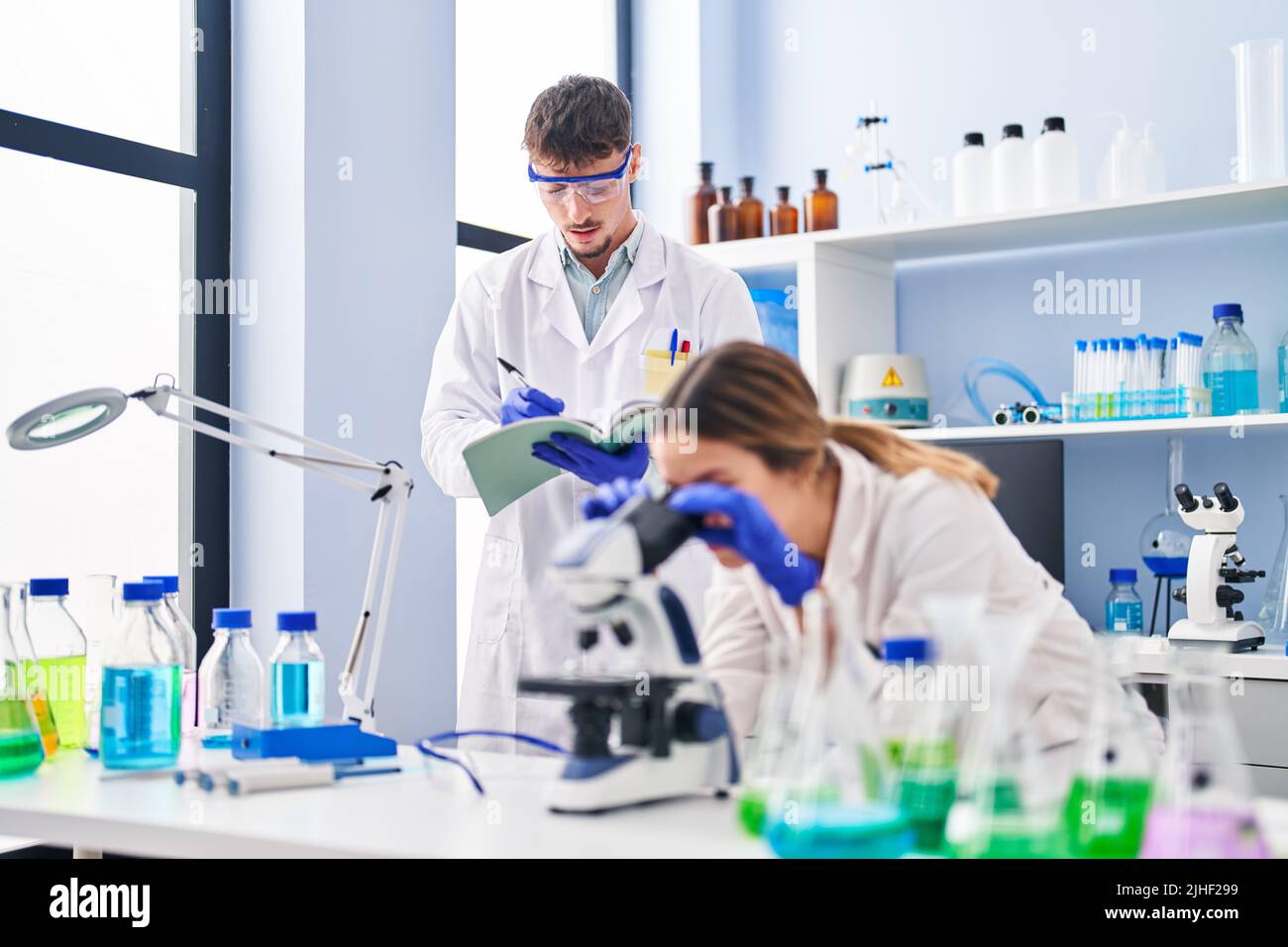 Young man and woman scientists workers using microscope at laboratory ...