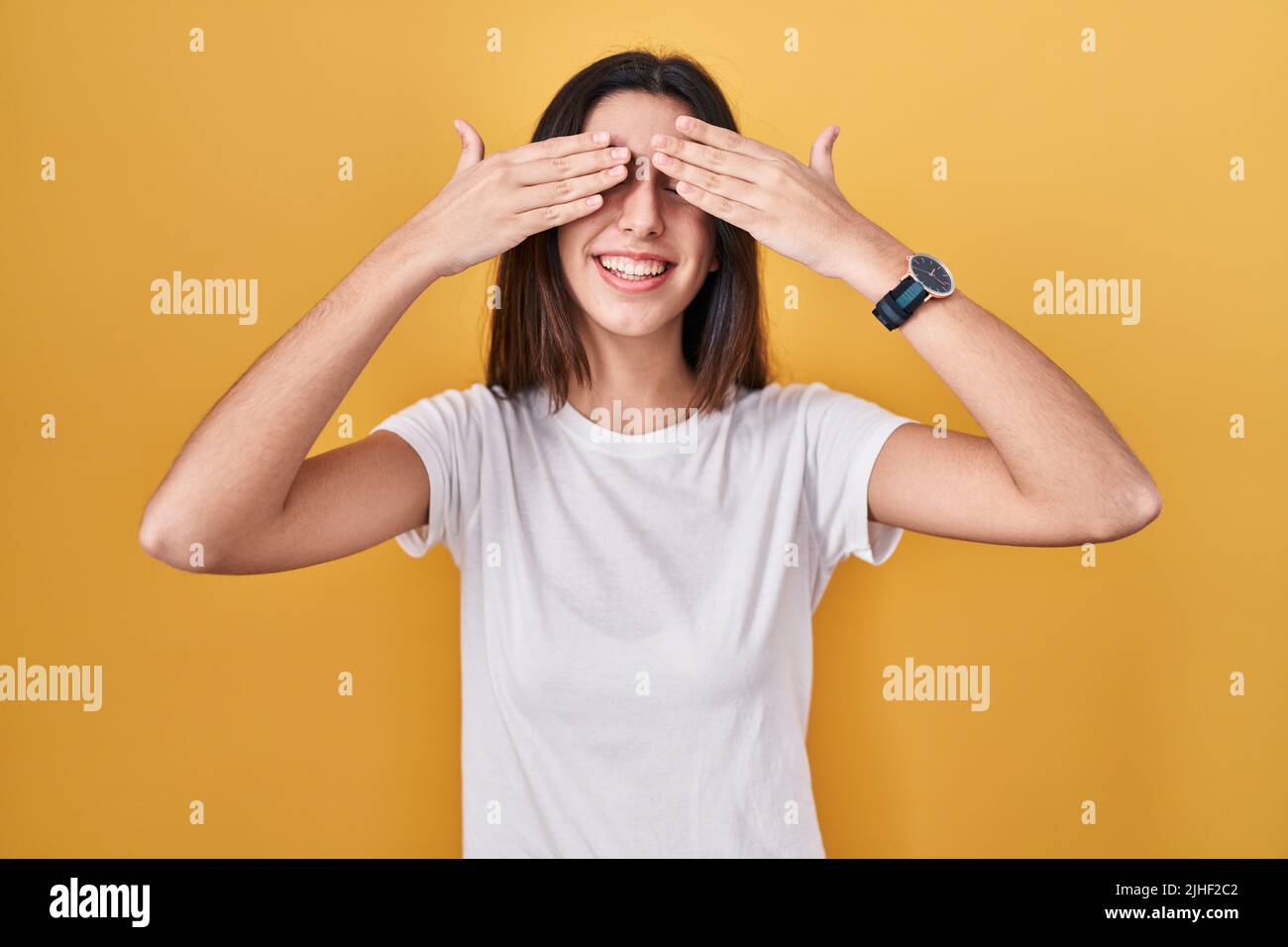 Young beautiful woman standing over yellow background covering eyes ...