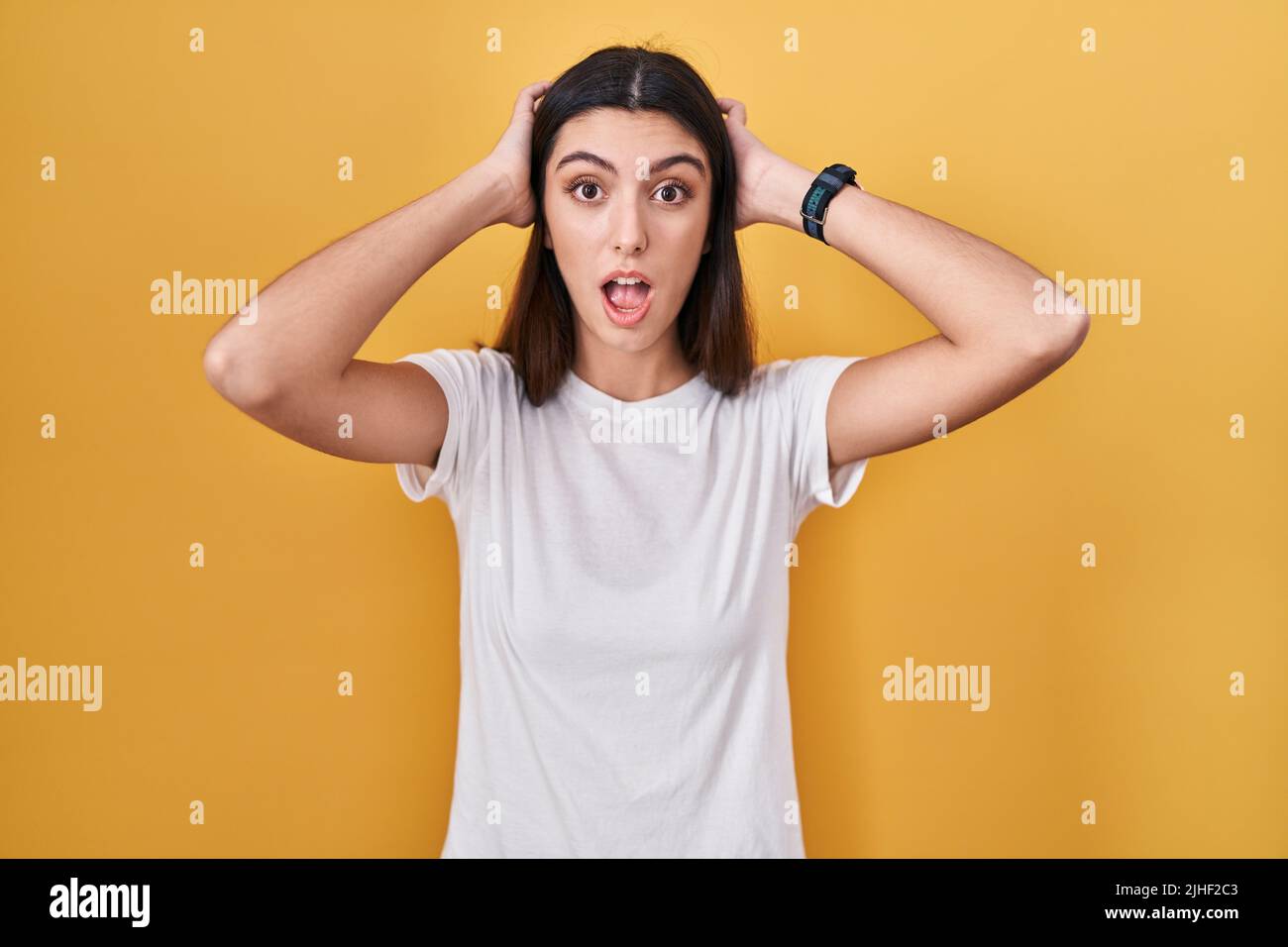 Young beautiful woman standing over yellow background crazy and scared ...