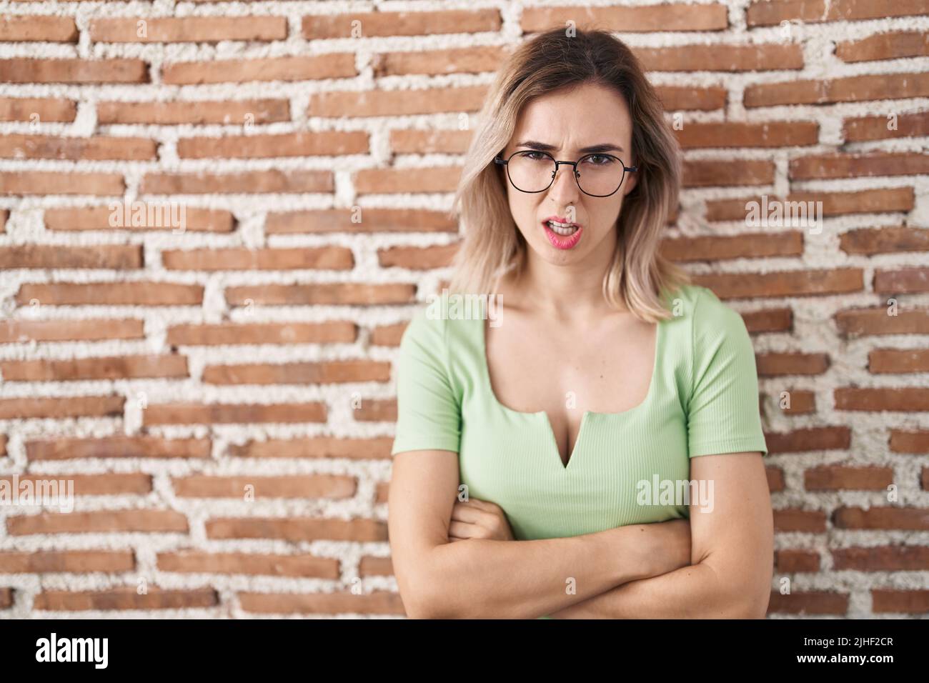 Young beautiful woman standing over bricks wall skeptic and nervous ...