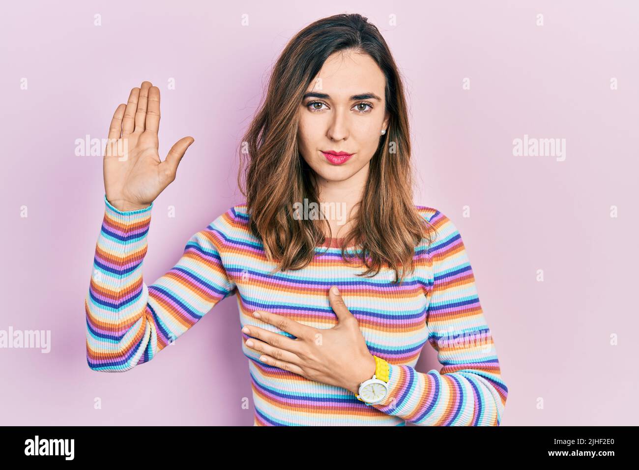 Young hispanic girl wearing casual clothes swearing with hand on chest ...