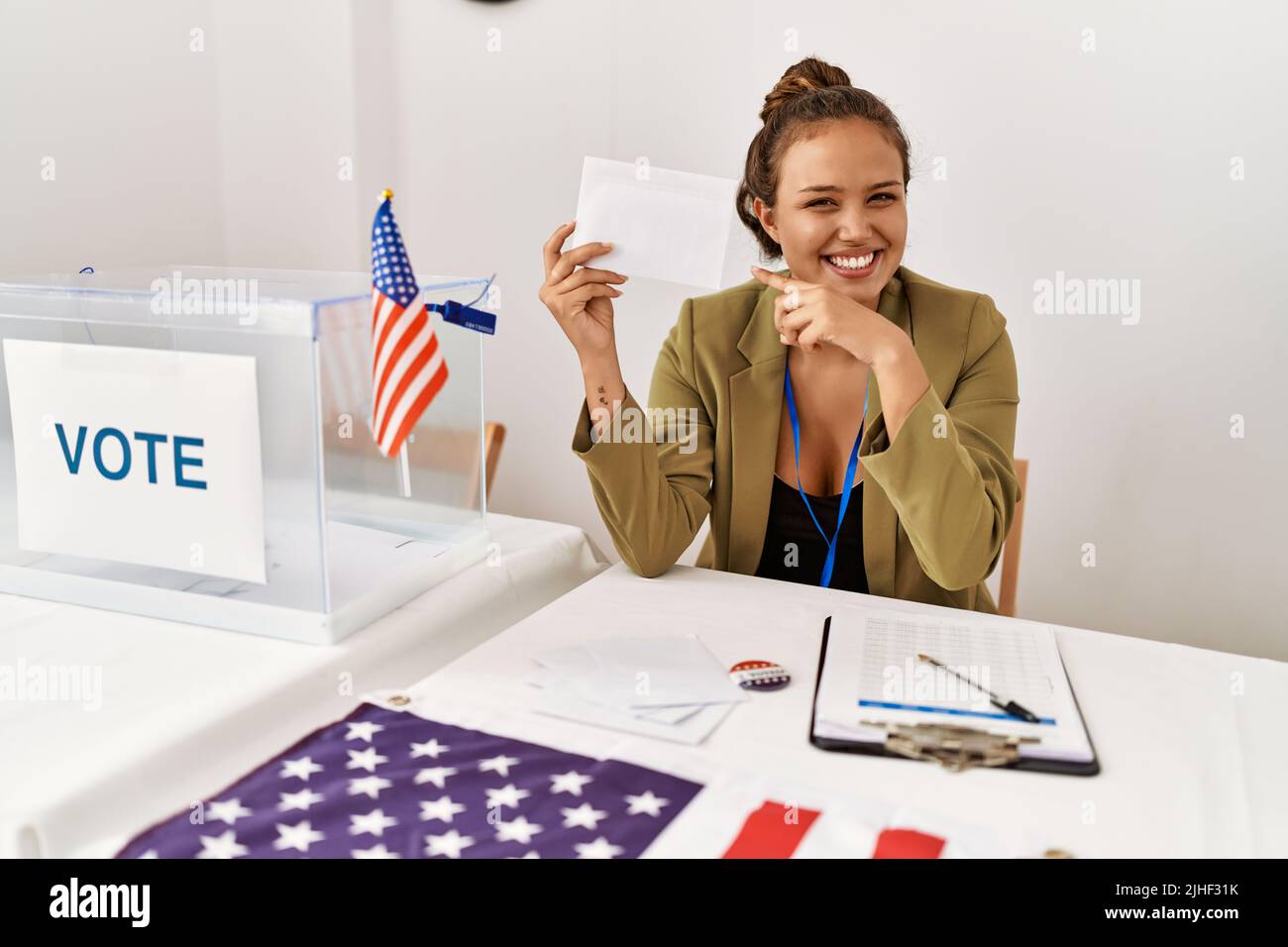 Beautiful hispanic woman holding voting envelop in ballot box smiling ...