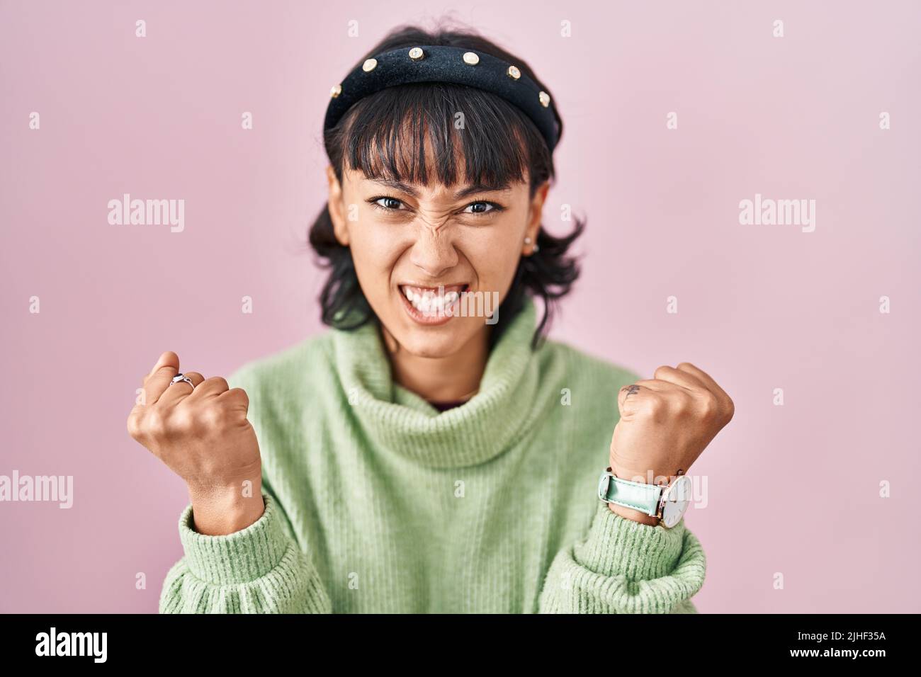 Young beautiful woman standing over pink background angry and mad ...