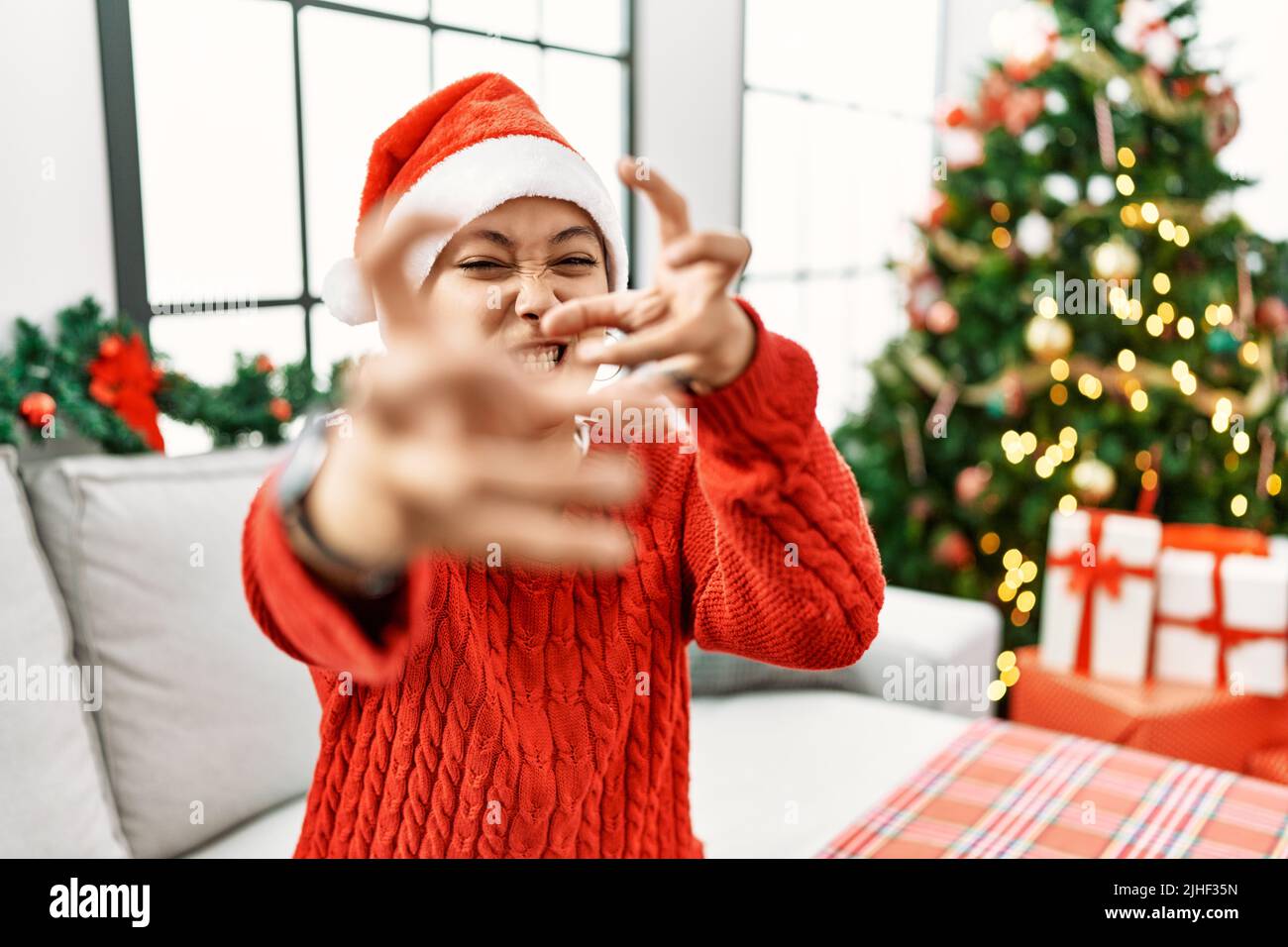 Young hispanic woman with short hair wearing christmas hat sitting on ...