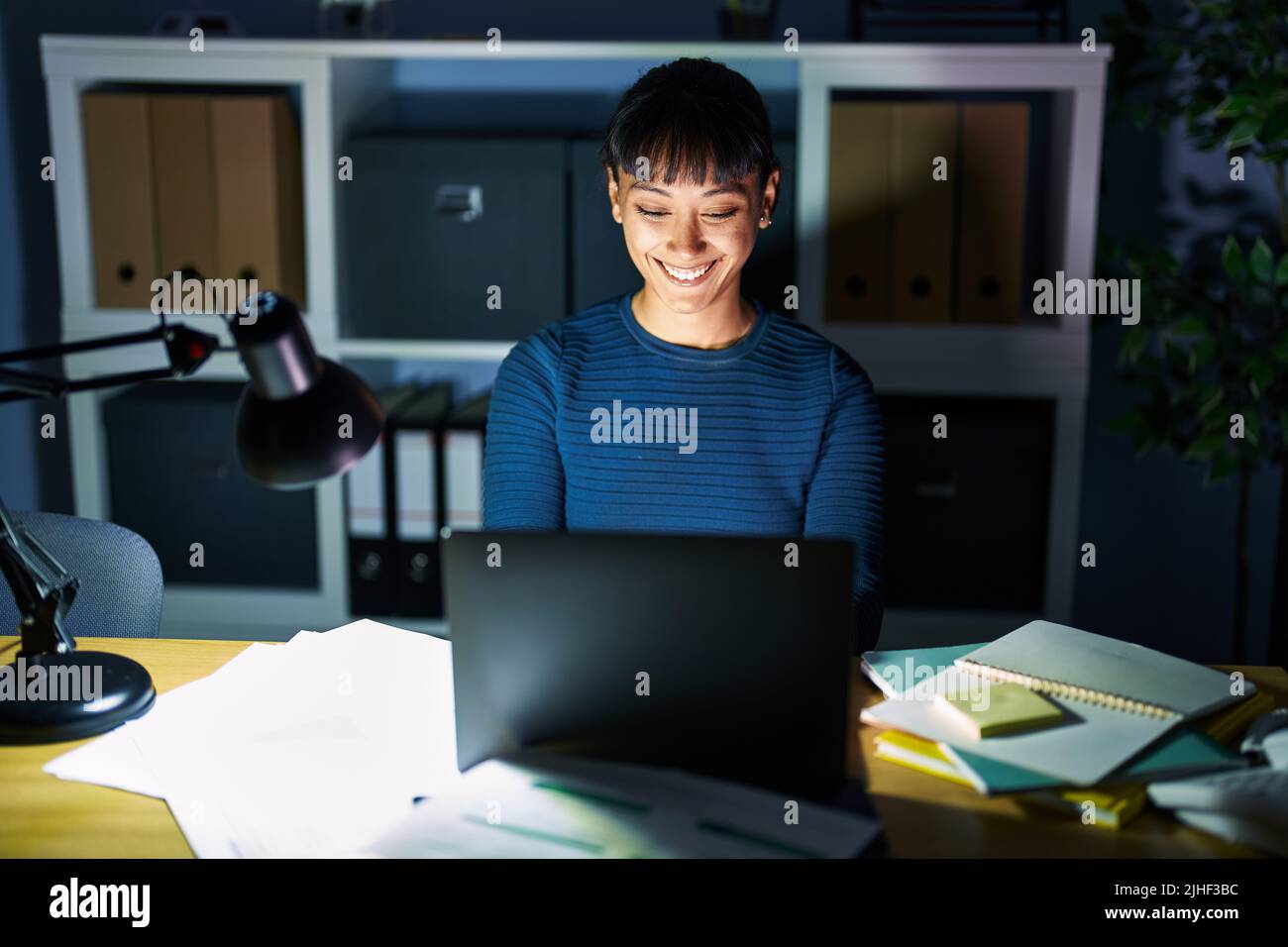 Young beautiful woman working at the office at night with a happy and ...