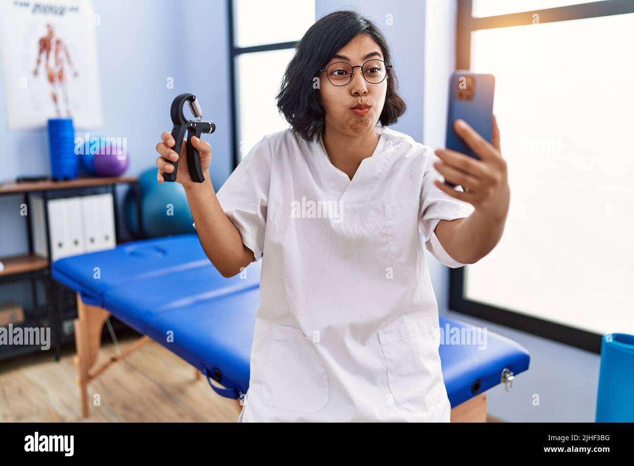Young hispanic physiotherapist woman holding hand grip to train muscle ...