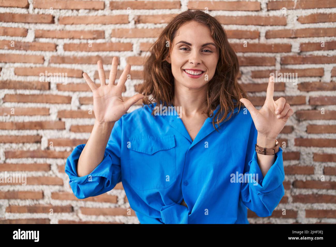 Beautiful Brunette Woman Standing Over Bricks Wall Showing And Pointing