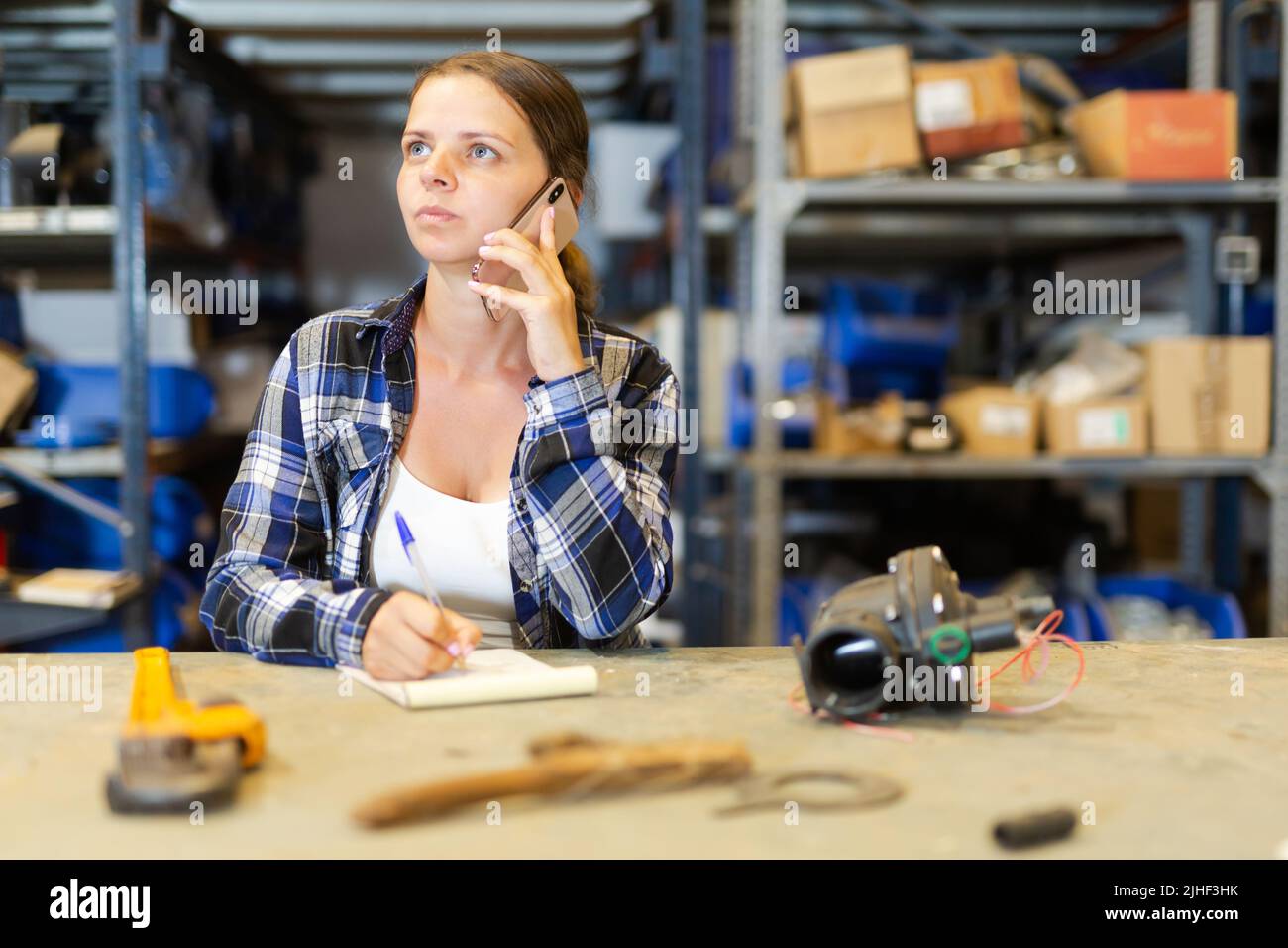 Young positive woman taking order at workplace talking mobile phone ...
