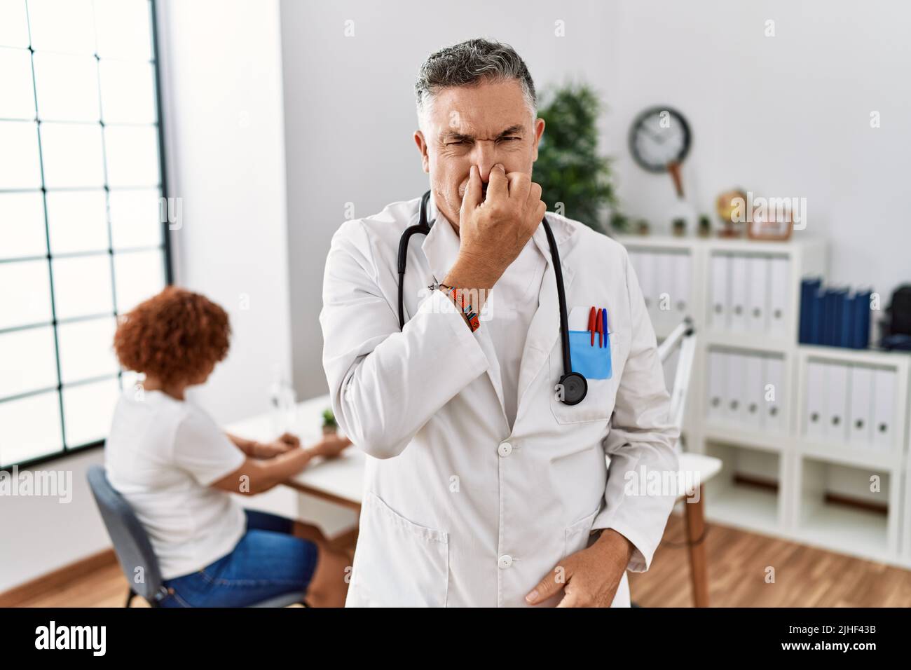 Middle age doctor man at the clinic with a patient smelling something ...