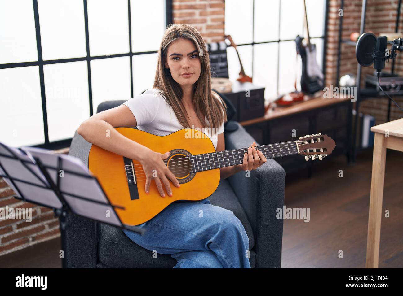 Young beautiful woman playing classic guitar at music studio thinking ...