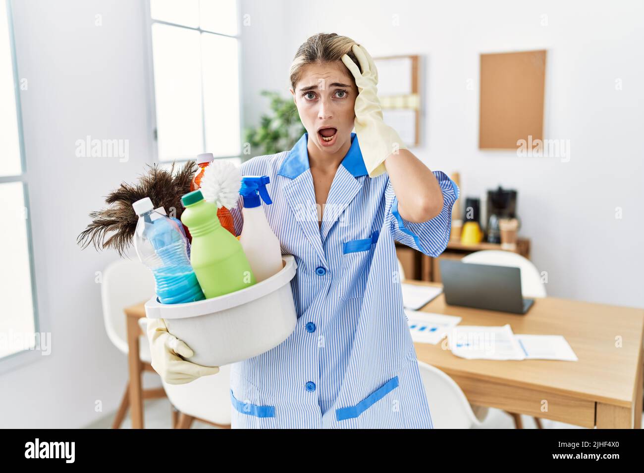 Young blonde woman wearing cleaner uniform holding cleaning products ...