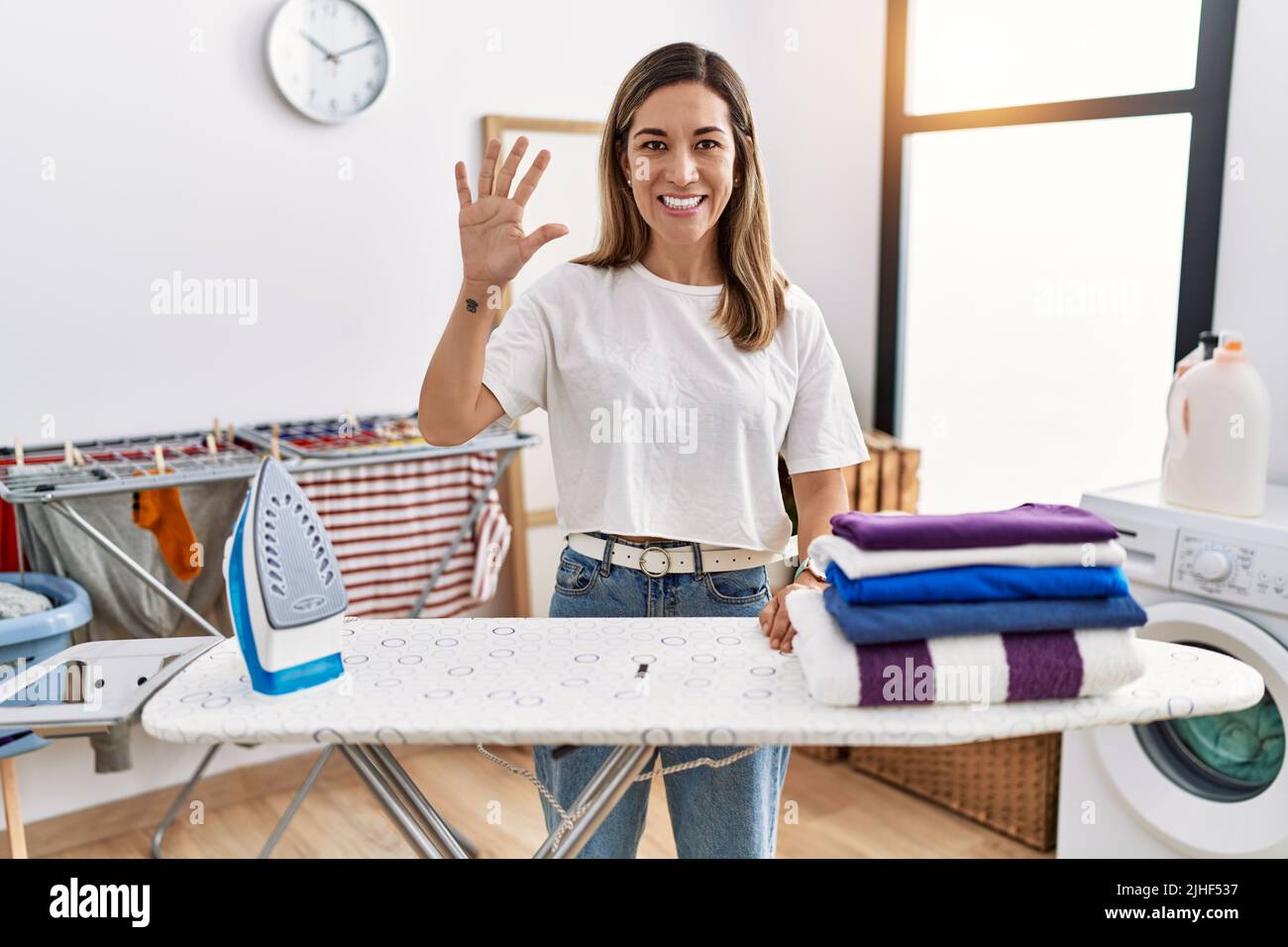 Young hispanic woman ironing clothes at laundry room showing and ...