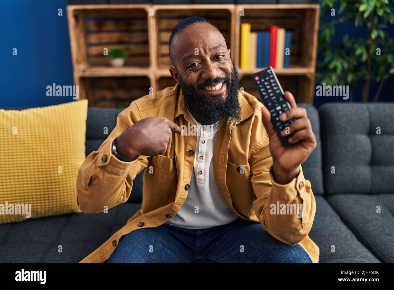 African american man holding television remote control pointing finger ...