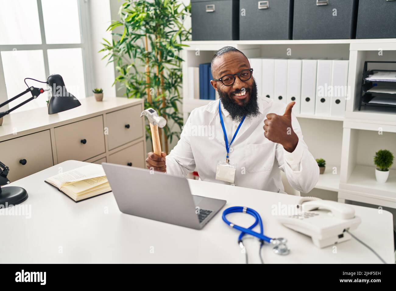 African american man working at medical clinic holding hammer smiling ...