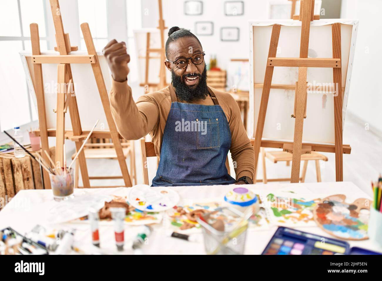 African american artist man at art studio angry and mad raising fist ...