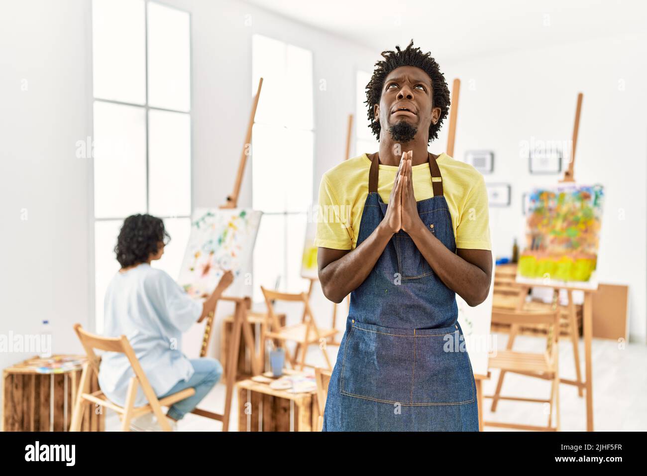 African young man standing at art studio begging and praying with hands ...