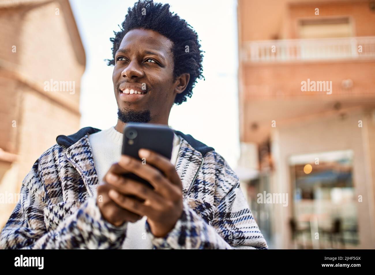 Handsome black man with afro hair smiling happy outdoors using ...