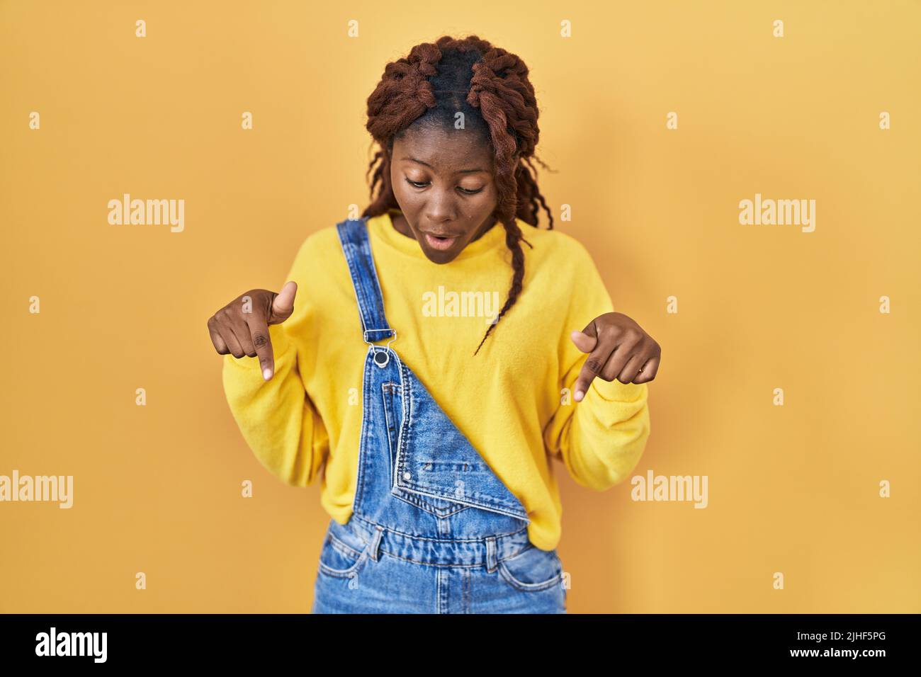African woman standing over yellow background pointing down with ...
