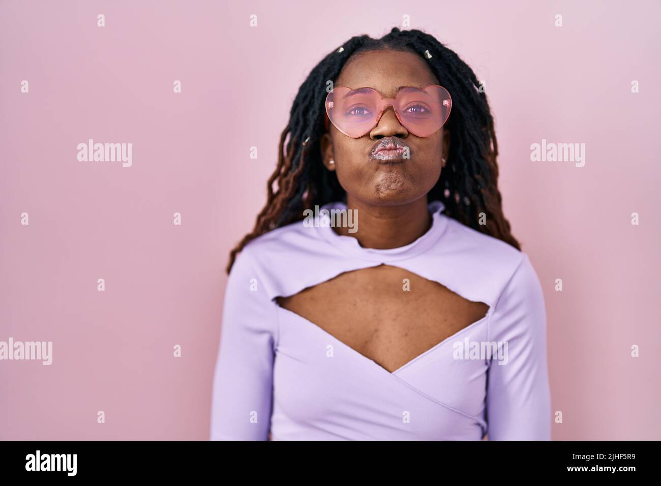 African woman with braided hair standing over pink background puffing ...