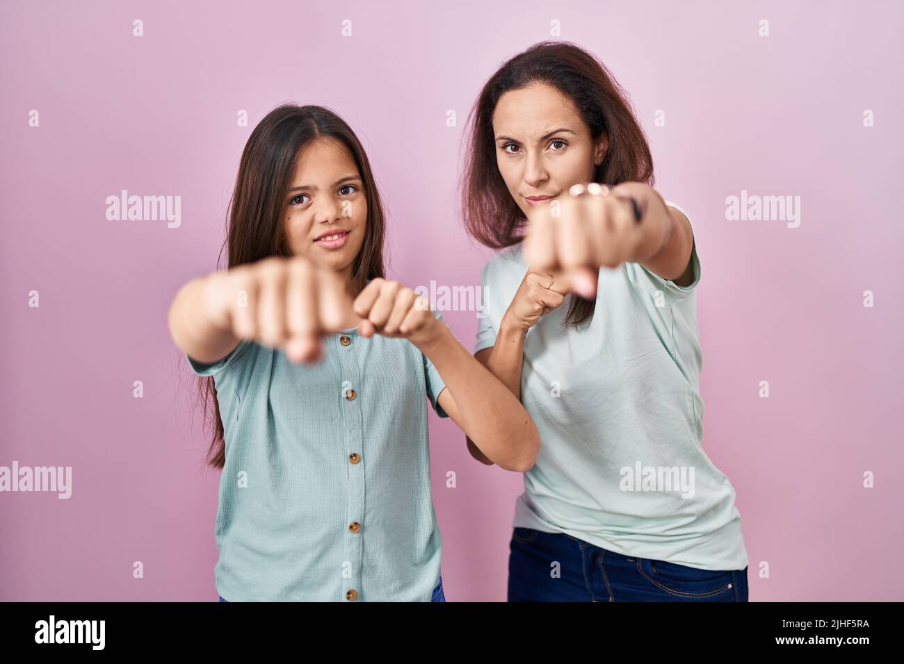 Young mother and daughter standing over pink background punching fist ...