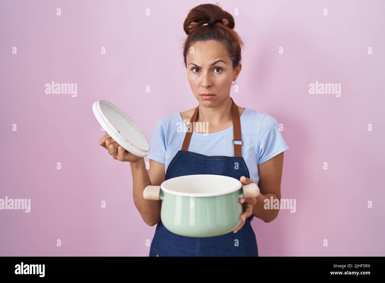 Brunette Woman Wearing Apron Holding Cooking Pot Skeptic And Nervous