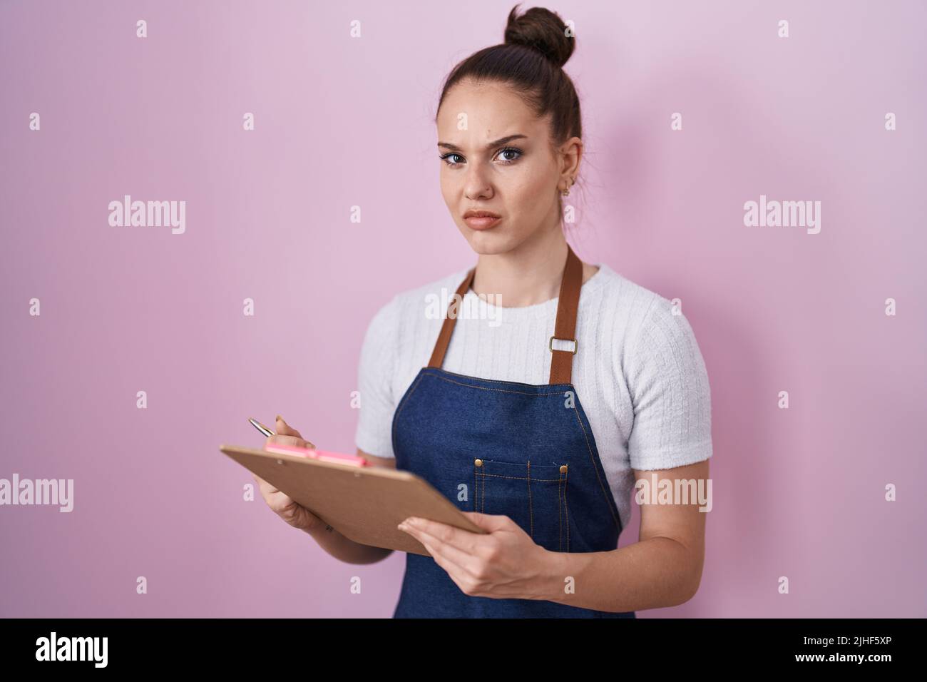 Young hispanic girl wearing professional waitress apron taking order ...