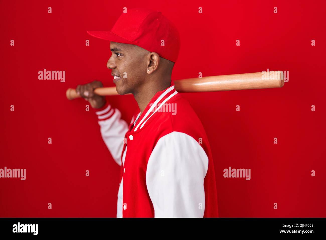 Young hispanic man playing baseball holding bat looking to side, relax ...
