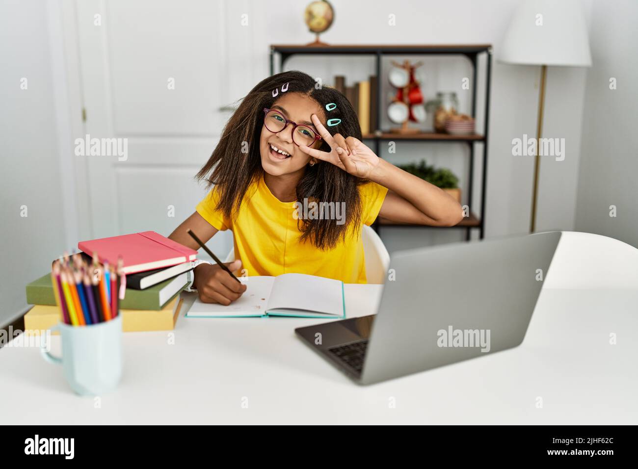 Young african american girl doing homework at home doing peace symbol ...