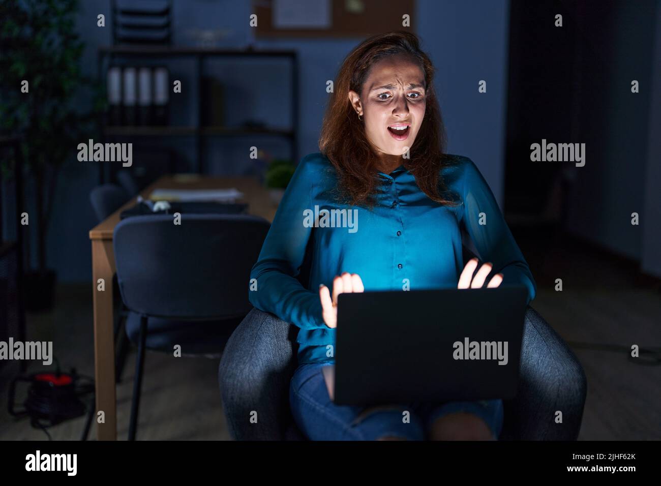 Brunette woman working at the office at night afraid and terrified with ...