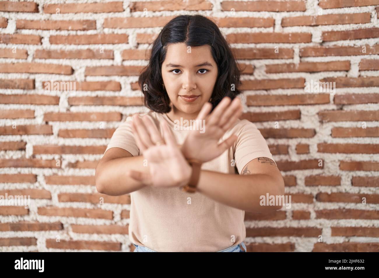 Young hispanic woman standing over bricks wall rejection expression ...