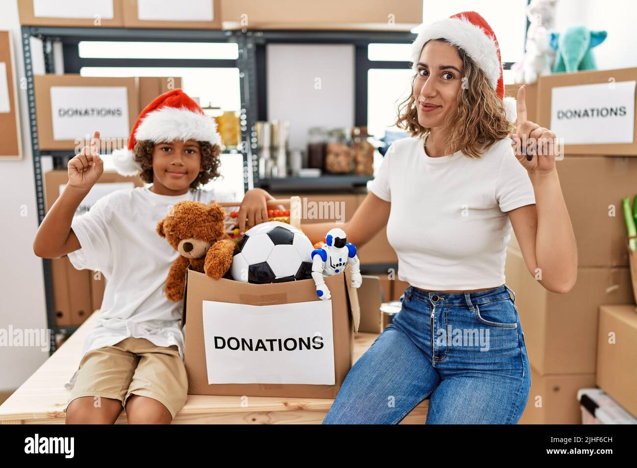 Young mother with little son wearing christmas hat at donations stand surprised with an idea or ...