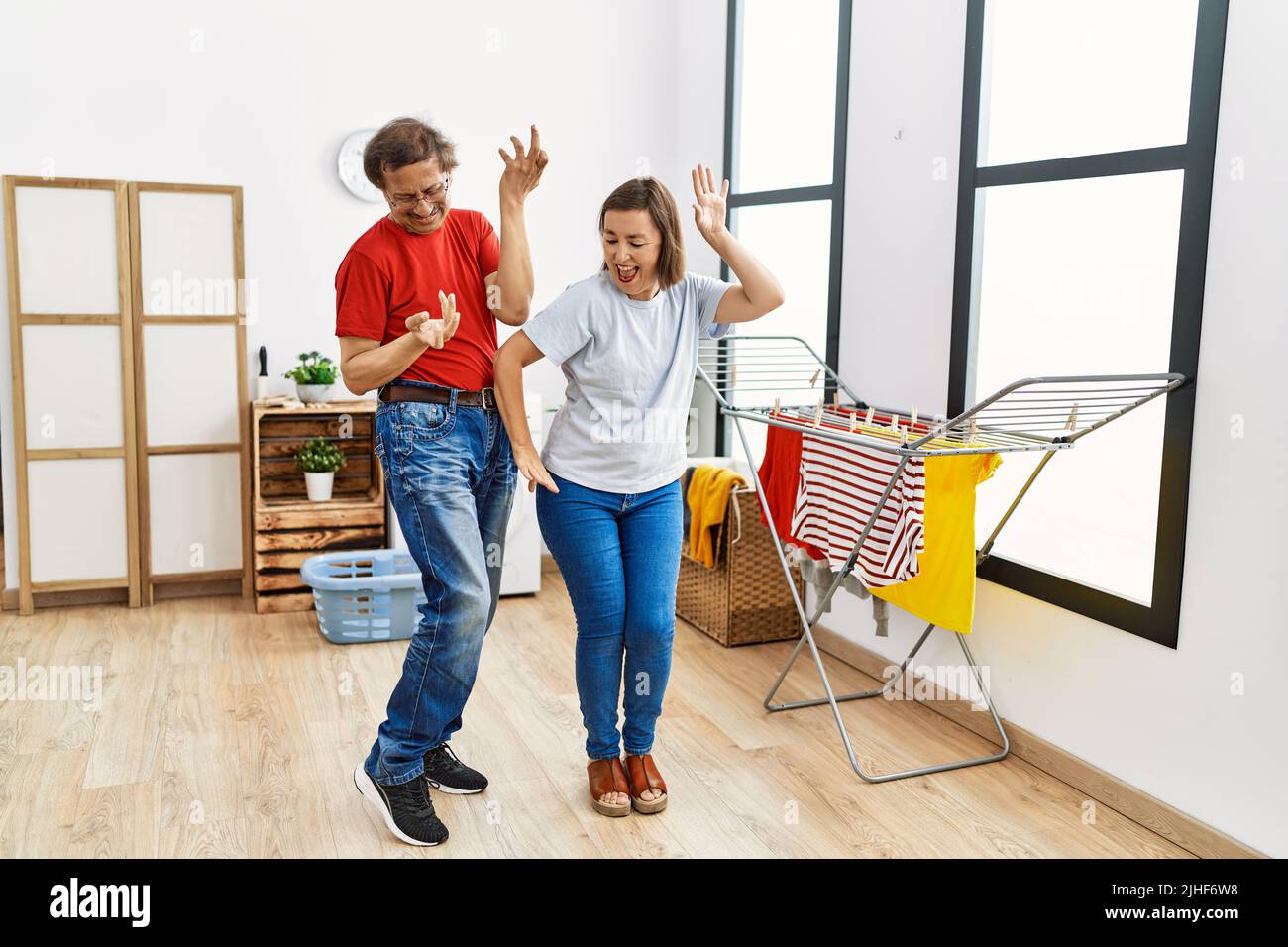 Middle age man and woman couple dancing waiting for washing machine at ...