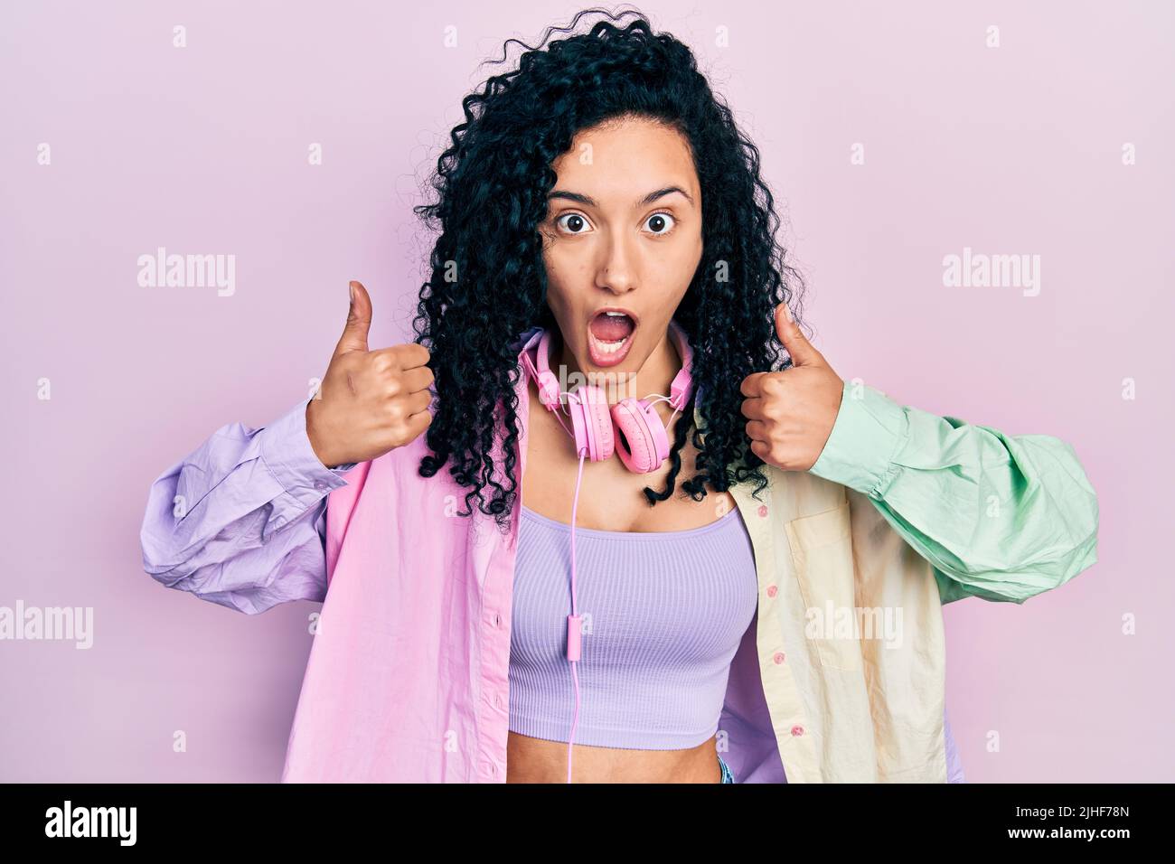 Young hispanic woman with curly hair doing thumbs up positive gesture ...