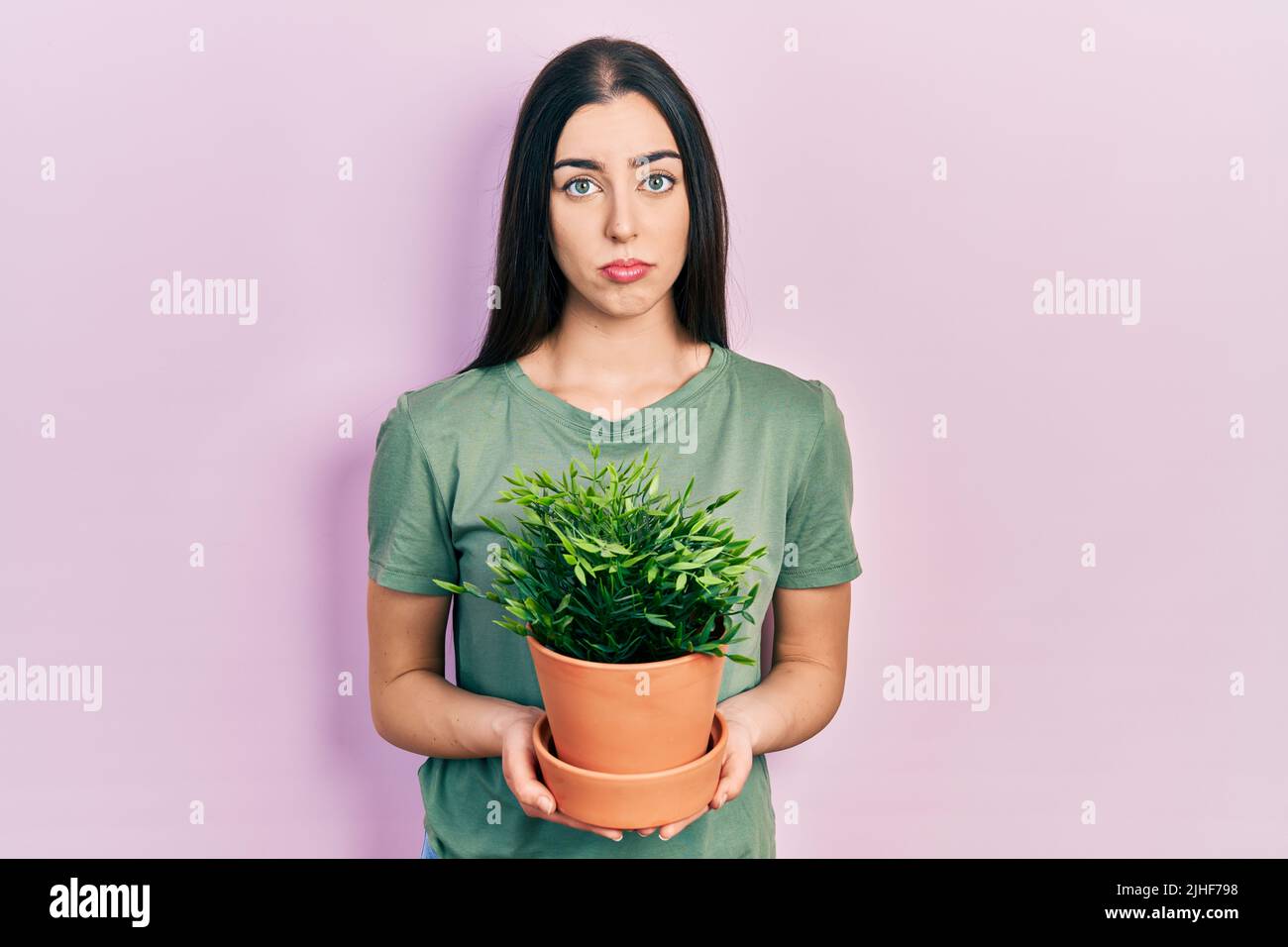 Beautiful woman with blue eyes holding green plant pot depressed and ...