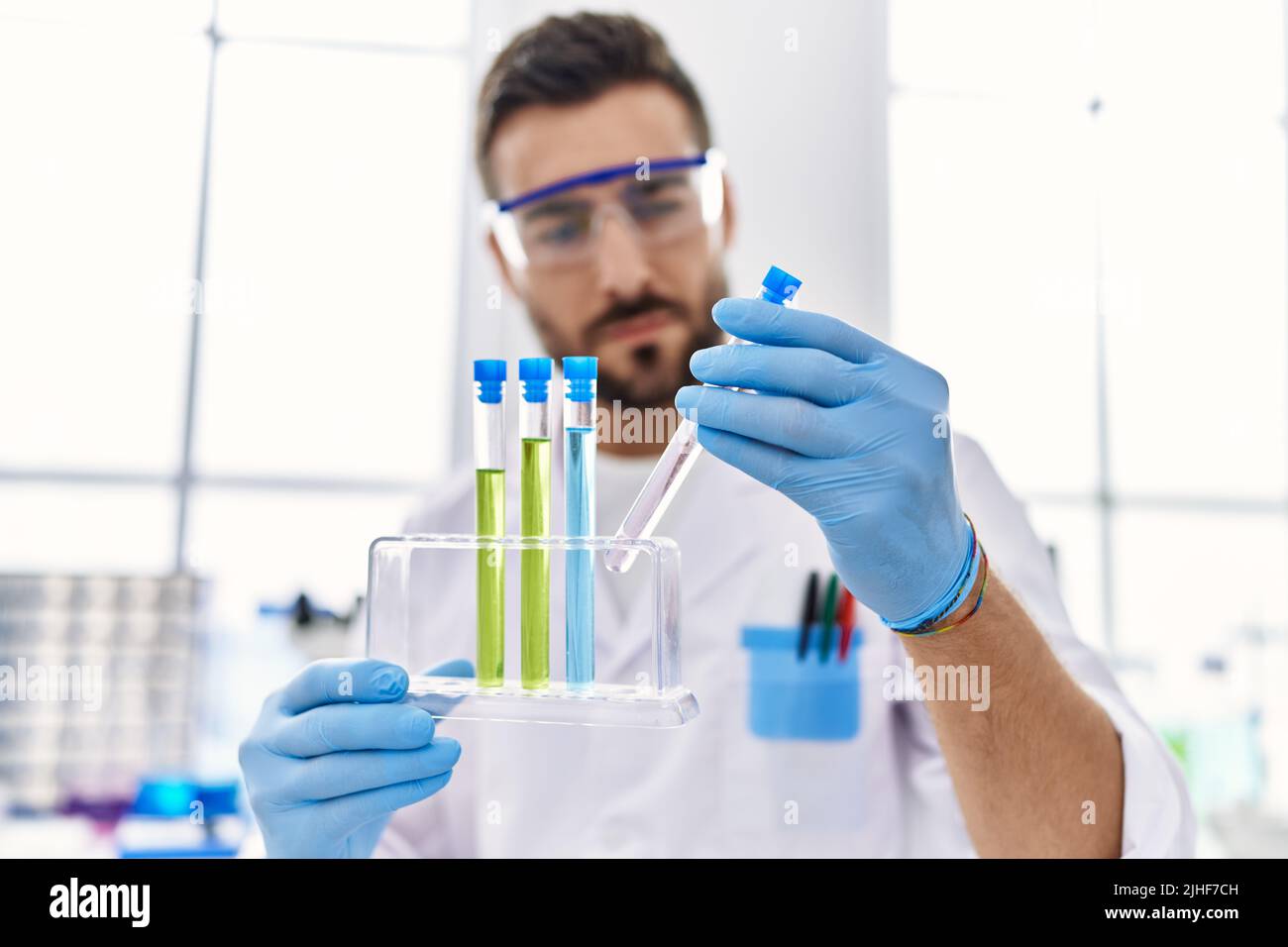 Young hispanic man wearing scientist uniform holding test tube at ...