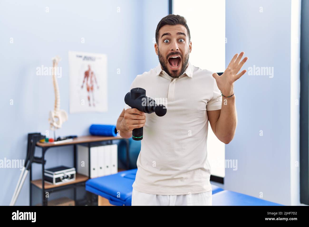 Handsome hispanic man holding therapy massage gun at physiotherapy ...