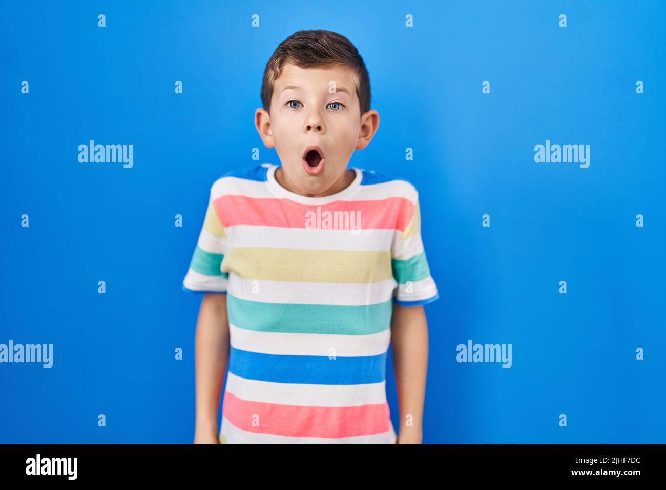 Young caucasian kid standing over blue background afraid and shocked ...