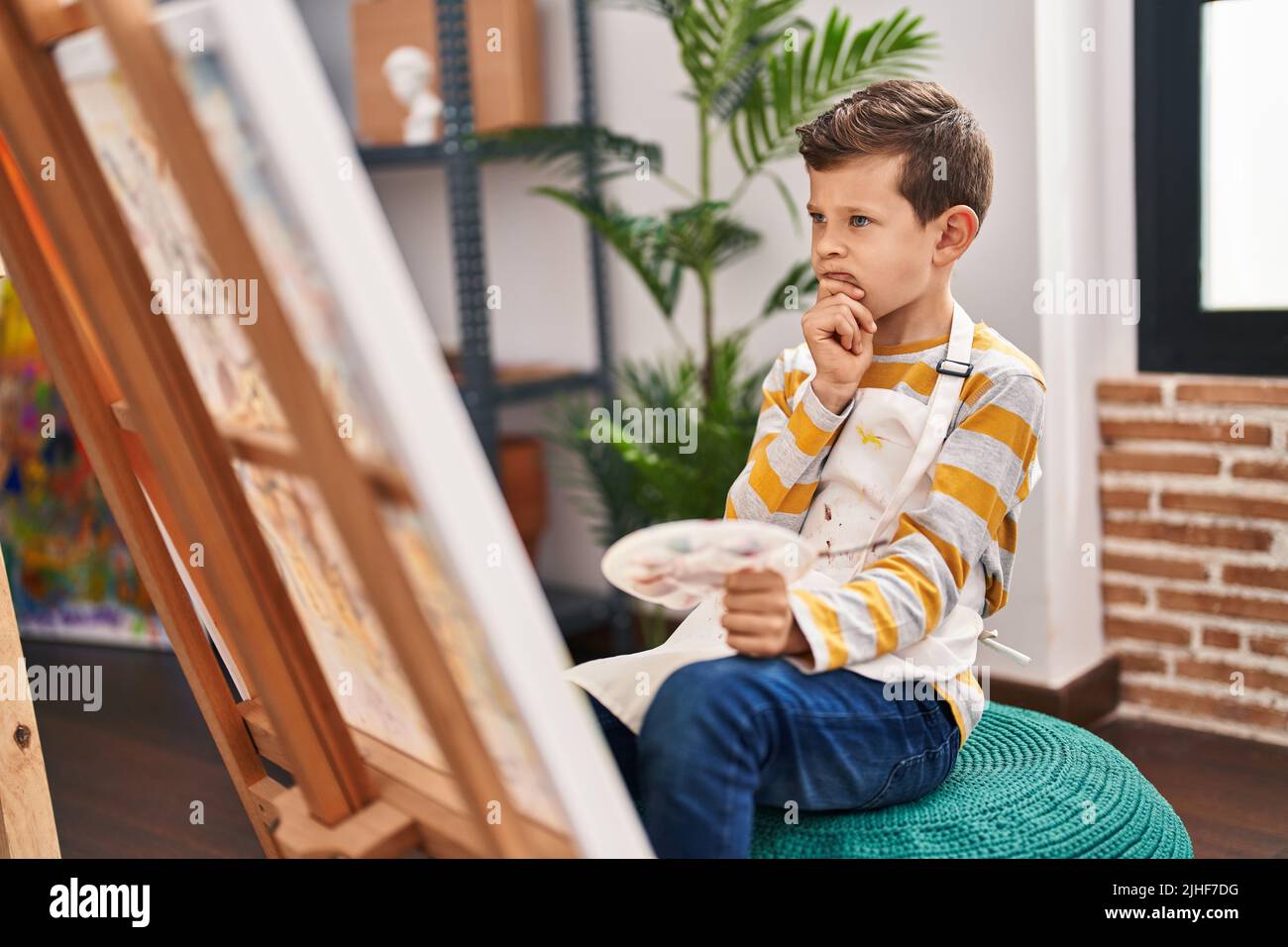 Blond child drawing with doubt expression at art studio Stock Photo - Alamy