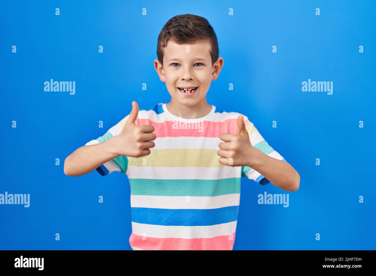 Young caucasian kid standing over blue background success sign doing ...