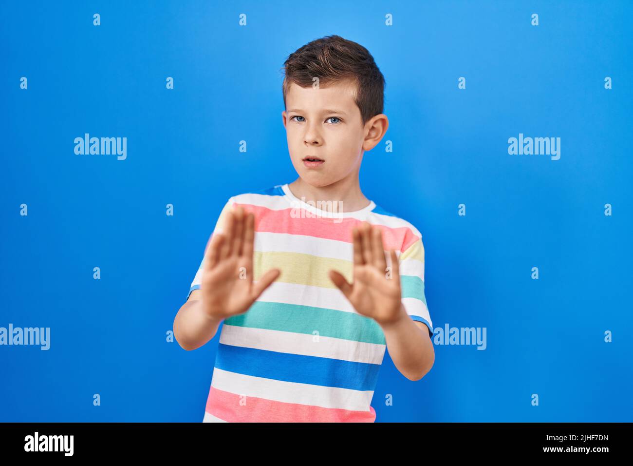 Young caucasian kid standing over blue background moving away hands ...