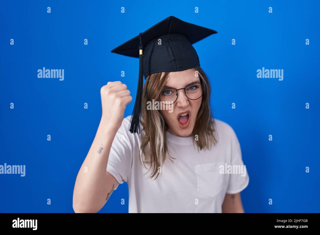 Blonde caucasian woman wearing graduation cap angry and mad raising ...