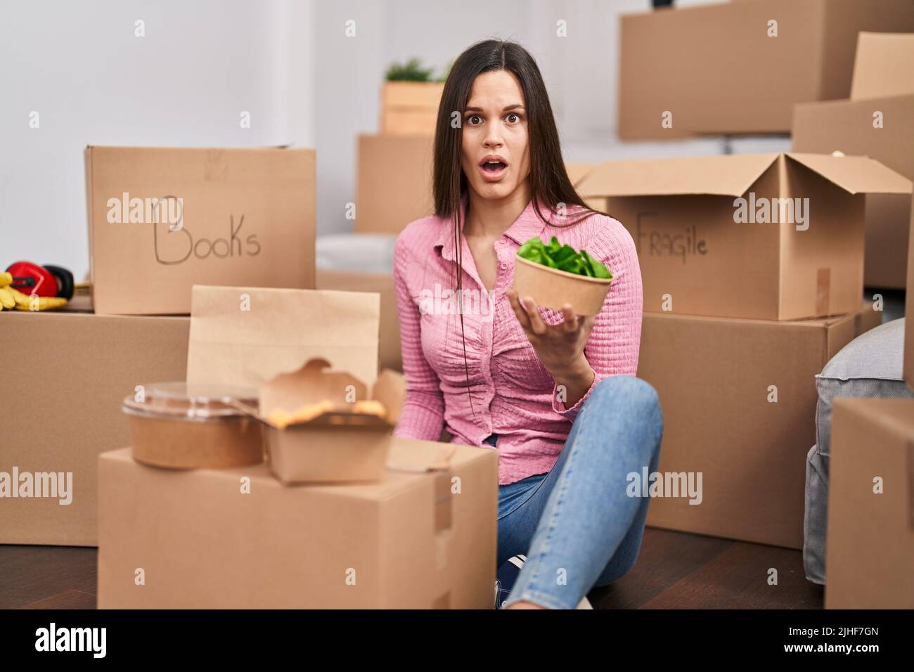 Young hispanic woman sitting on the floor at new home eating delivery ...