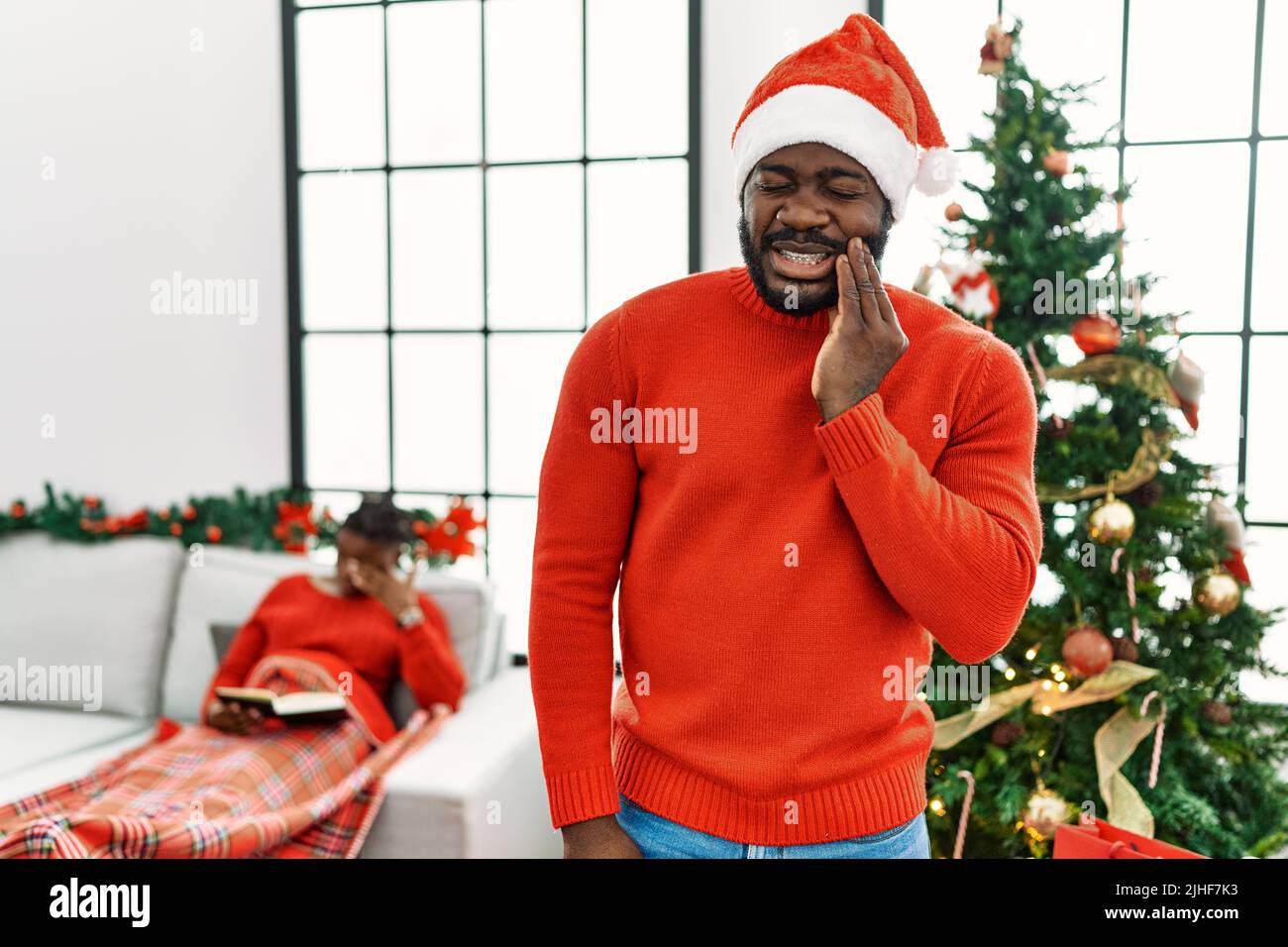 Young african american man standing by christmas tree touching mouth ...