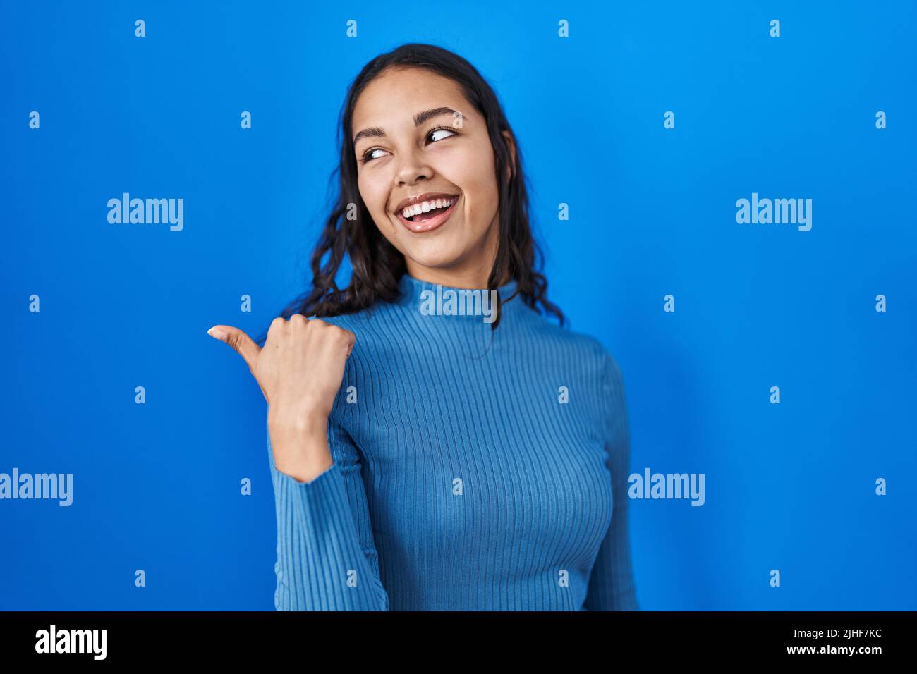 Young brazilian woman standing over blue isolated background smiling ...