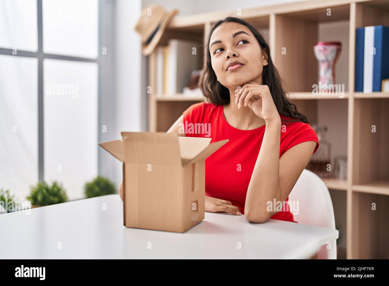 Young brazilian woman looking inside cardboard box smiling looking ...