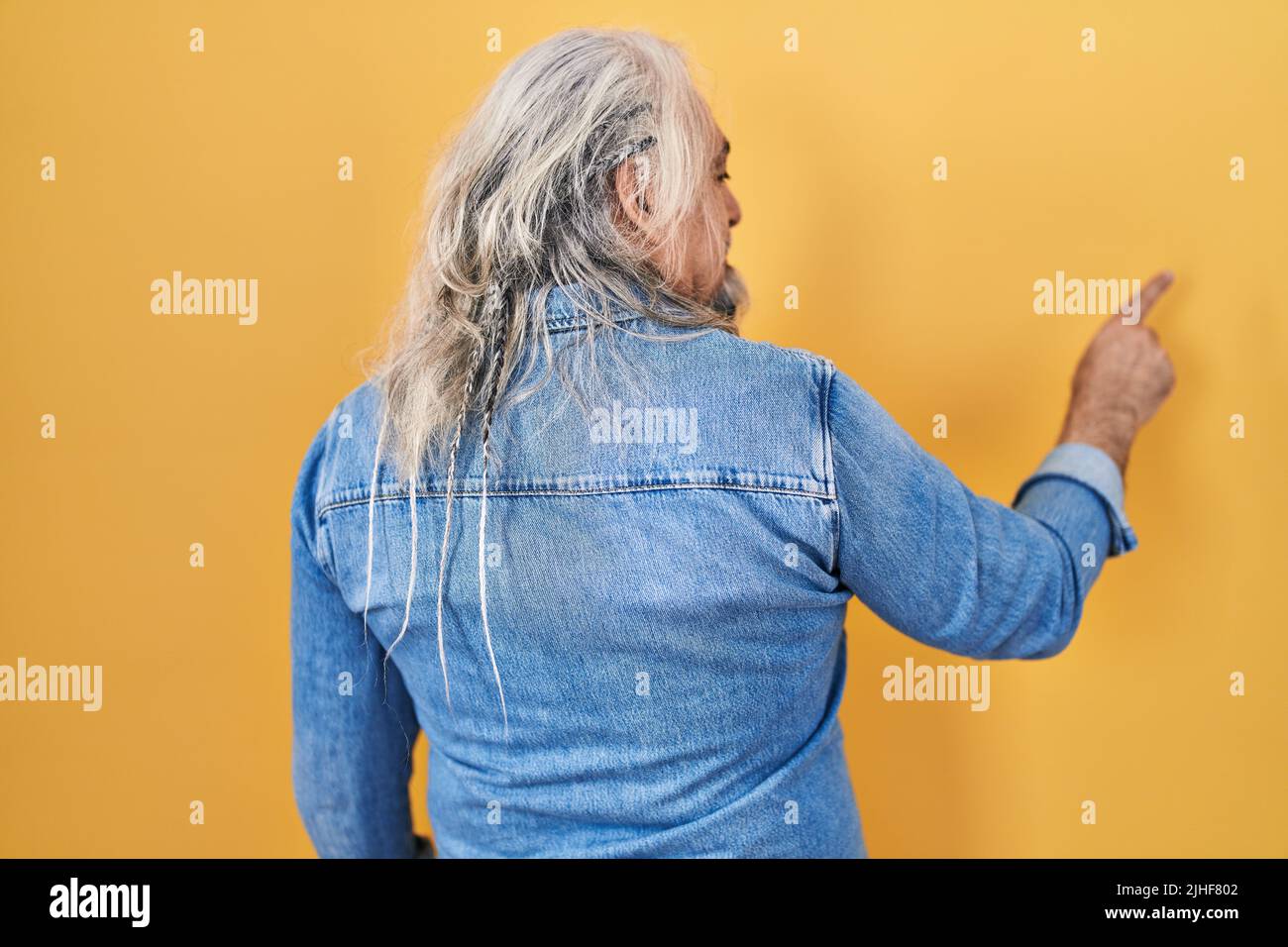 Middle age man with grey hair standing over yellow background posing ...