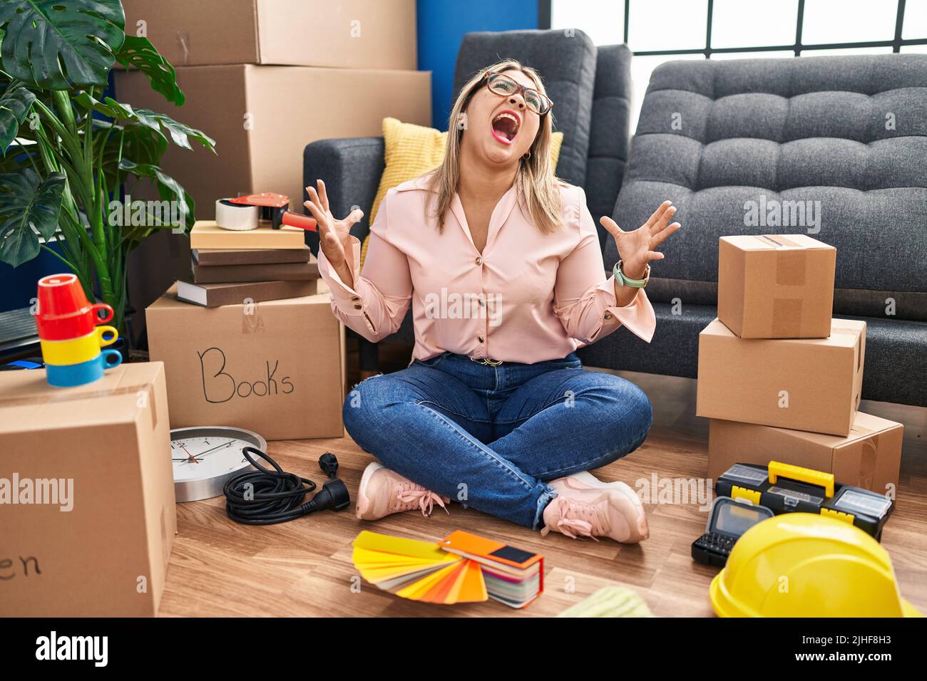 Young hispanic woman moving to a new home sitting on the floor crazy ...