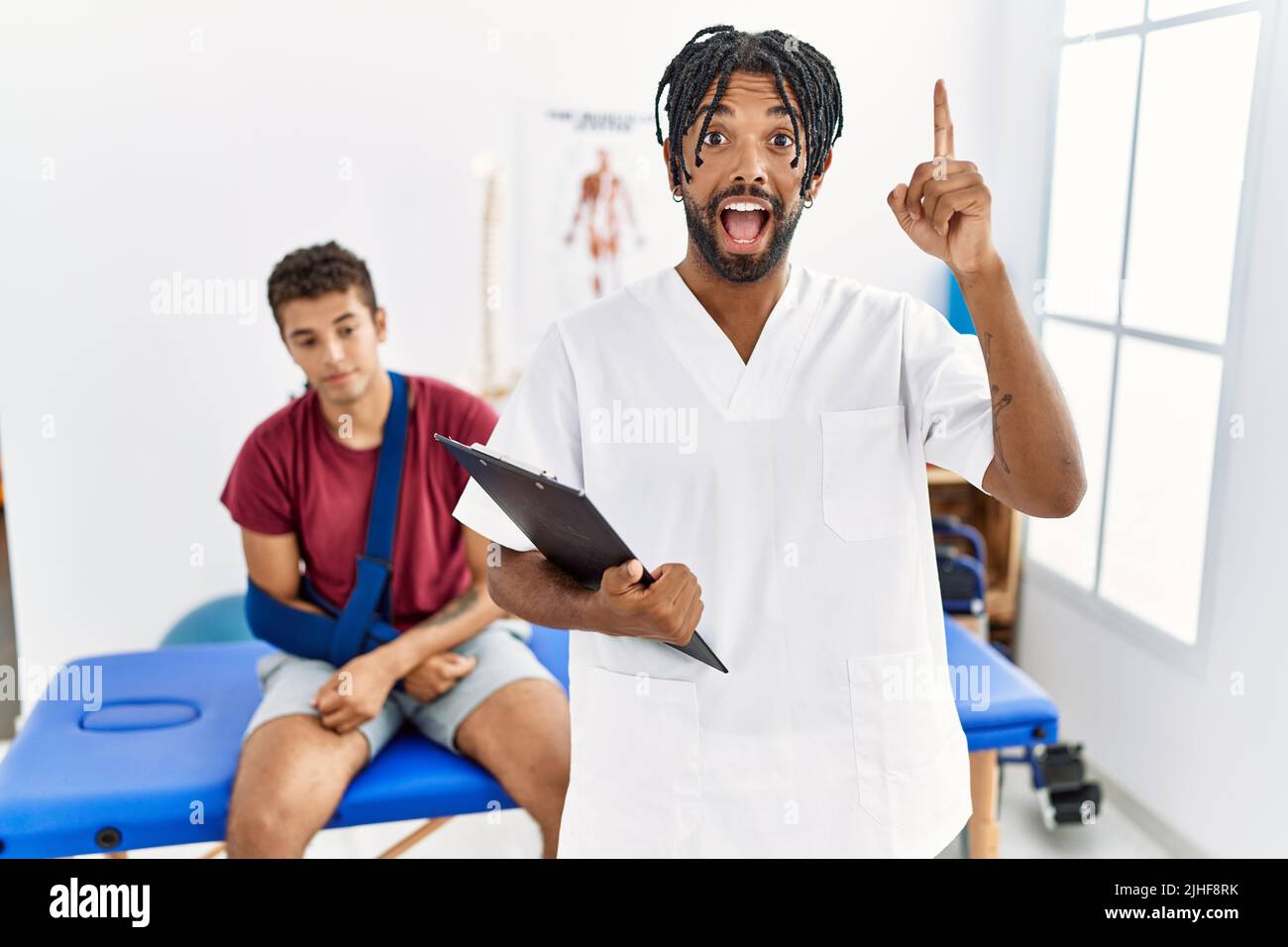 Young hispanic man working at pain recovery clinic with a man with ...